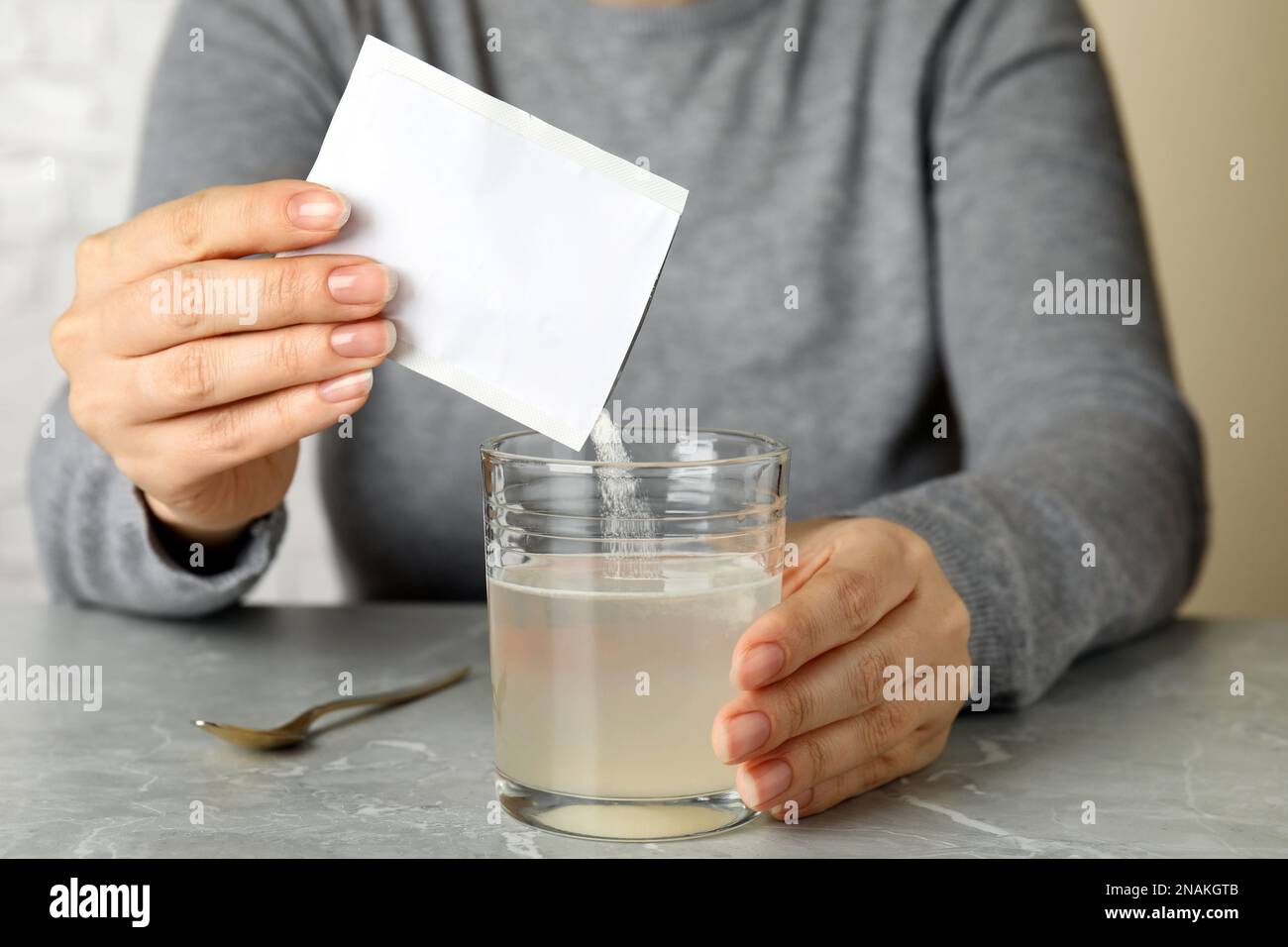 Woman pouring powder from medicine sachet into glass of water on grey ...