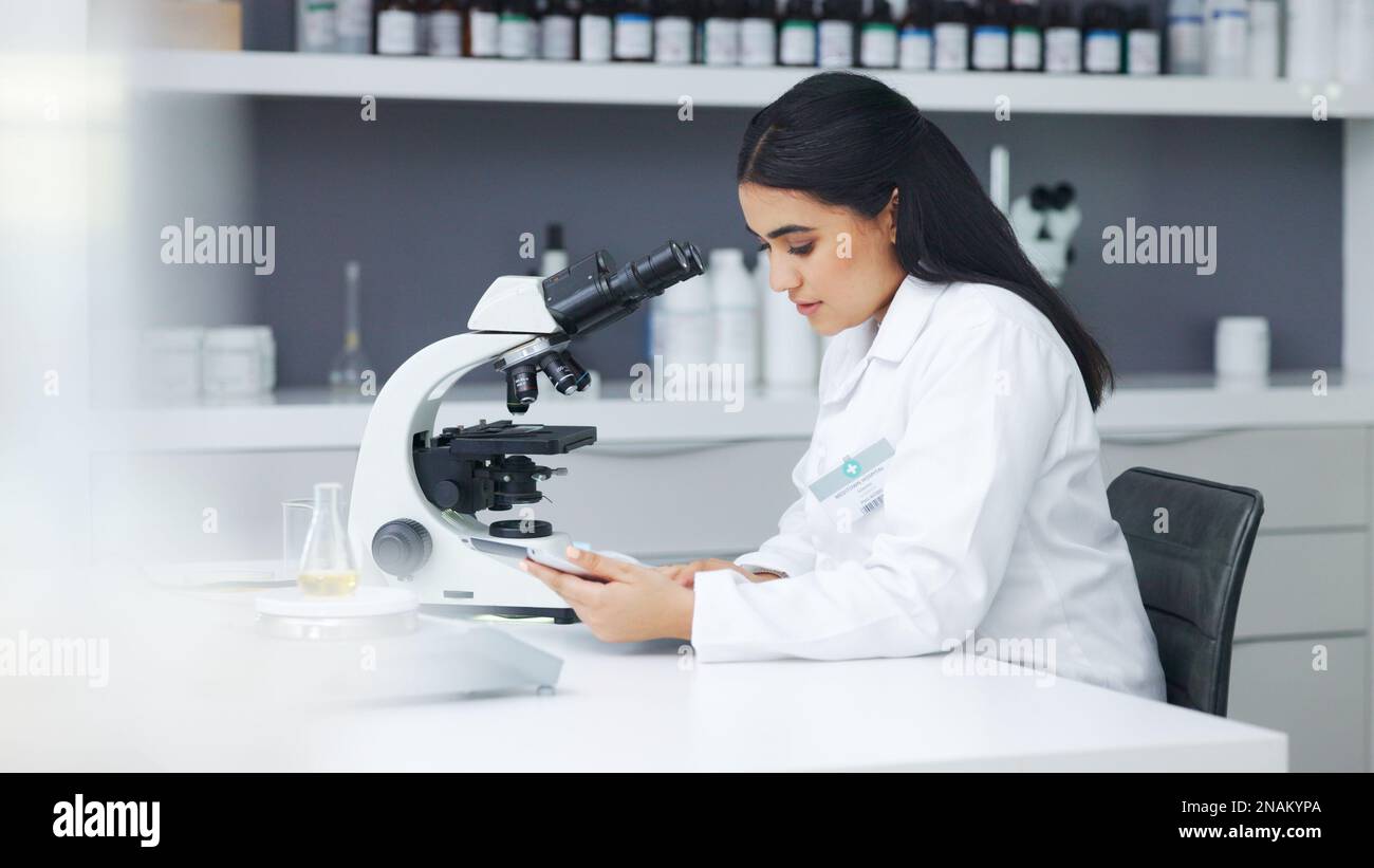 Young scientist using a digital tablet and microscope in a lab. Female pathologist analyzing ...