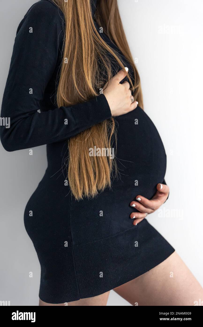 Stylish young pregnant woman in a black short dress on a white ...