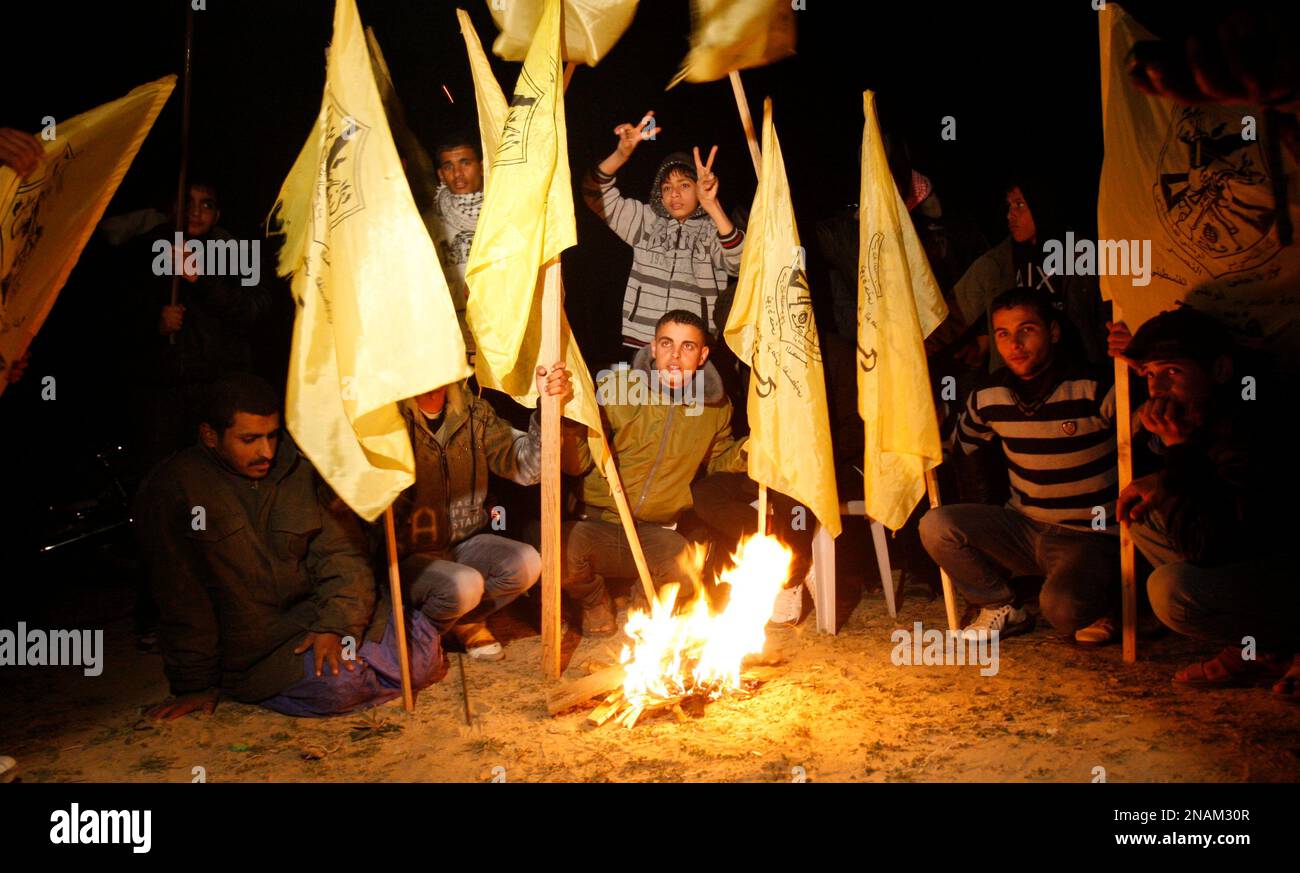 Palestinians gather around fire waving yellow Fatah flags as they wait ...