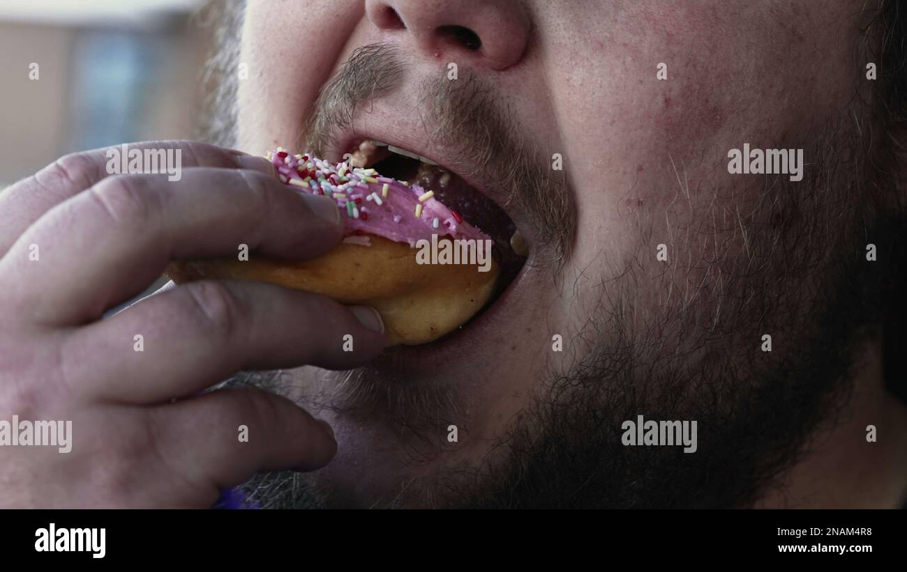 Chubby man eating unhealthy food. Person taking a bite of donut snack ...