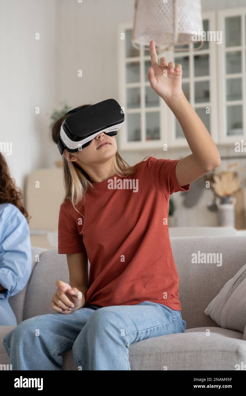 Curious teen girl child sitting on sofa using VR headset playing ...