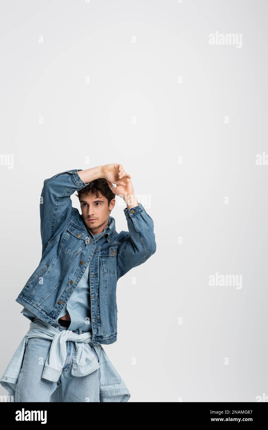 stylish young man in denim jacket and jeans posing with hands above ...