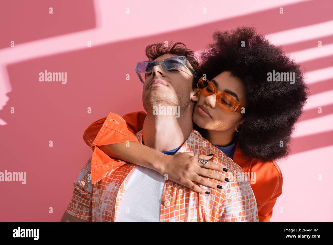 Stylish african american woman hugging man on pink background with ...