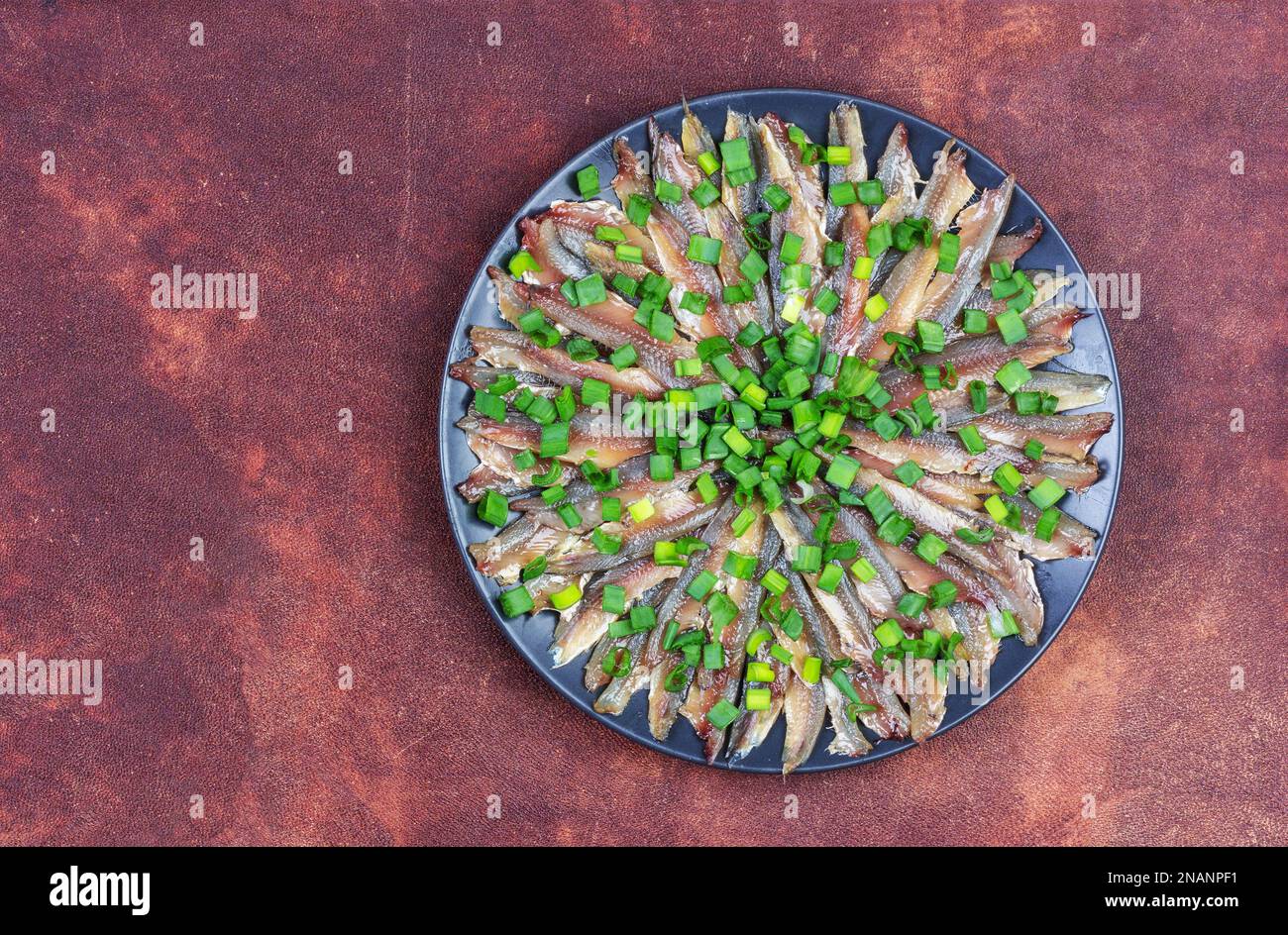 european anchovy fish fillet with green onion in a black plate on a red ...