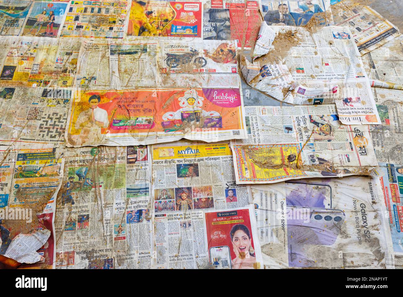 Colourful local newspaper pages laid out on a pavement in Fariapukur ...
