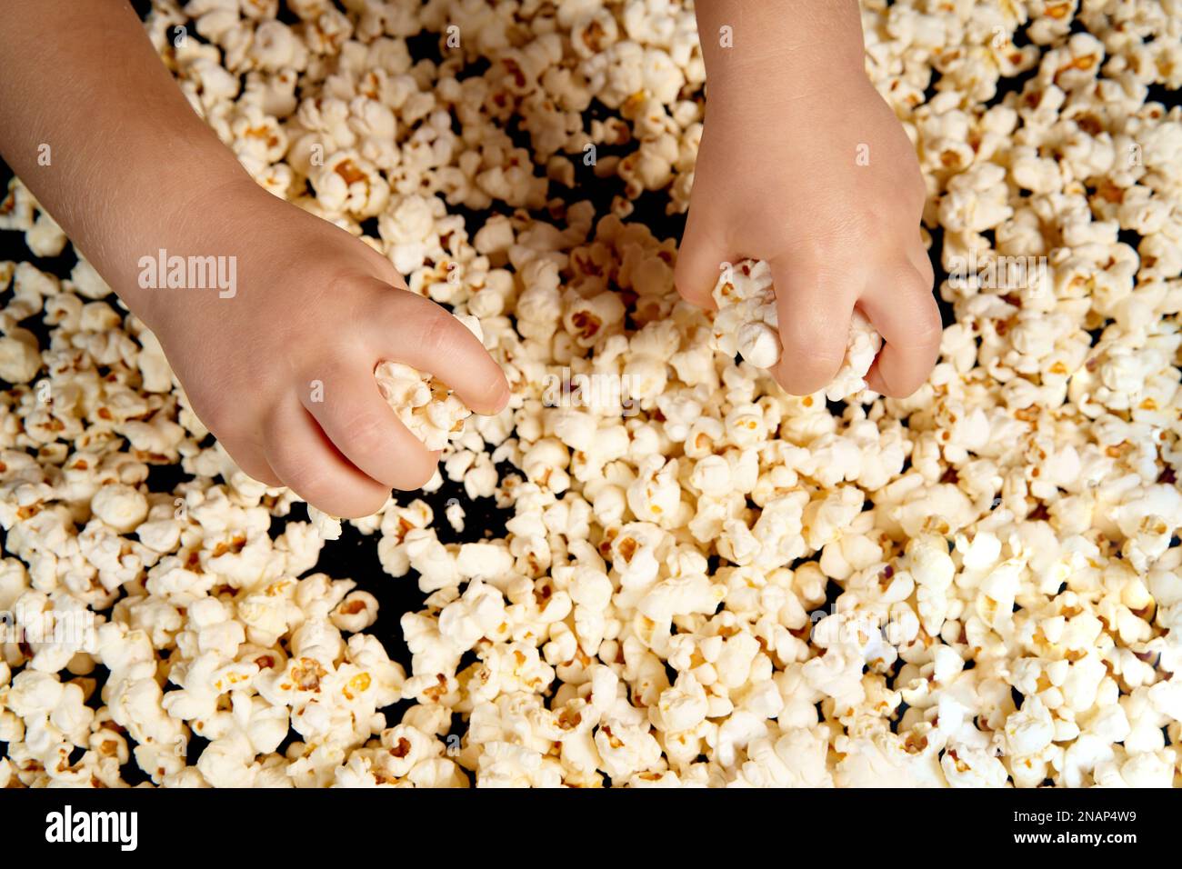 Children's hands are picking up popcorn. Flat lay . The concept of a ...