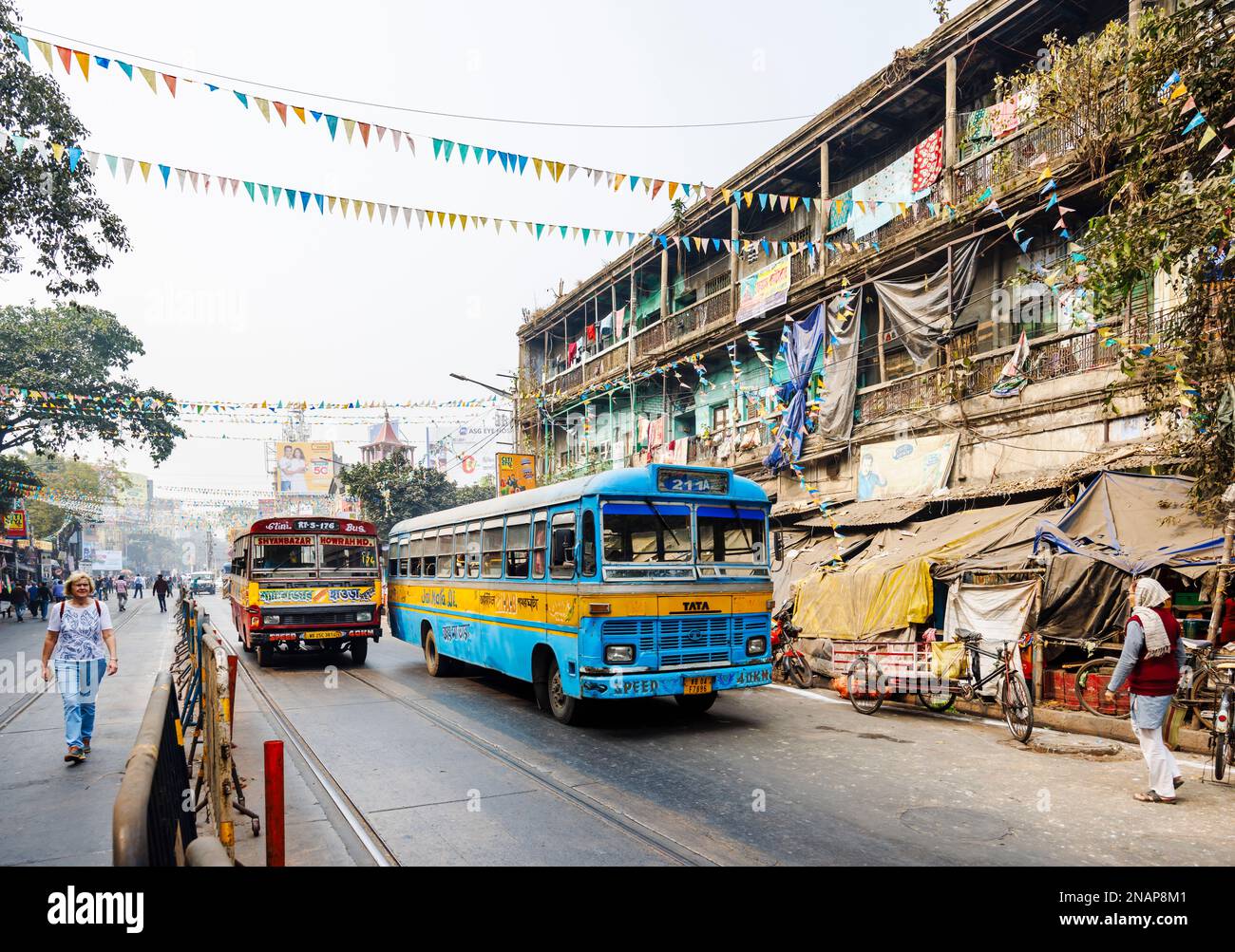 Street scene of buses passing shops, stalls and kiosks in the shopping ...