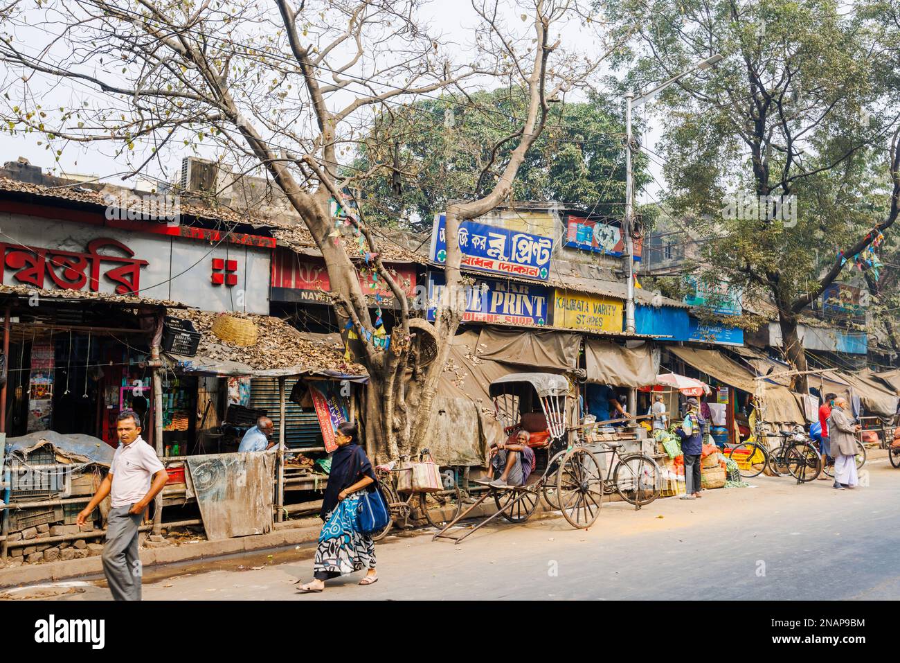 Street scene of a resting rickshaw driver, local people, shops, stalls ...