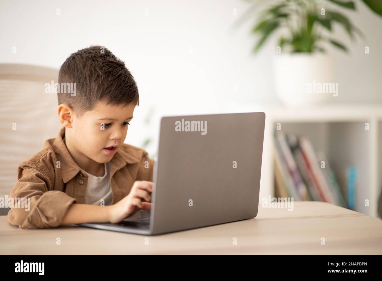 Busy cute european small kid typing on laptop at table, watch video ...