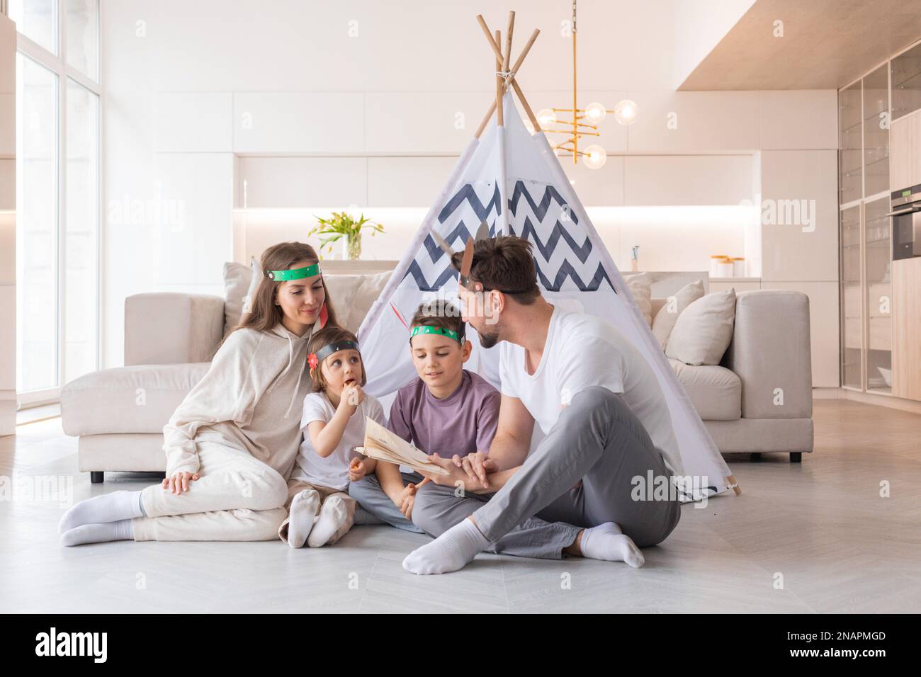 Happy family of parents and two children playing indian at home, wigwam ...