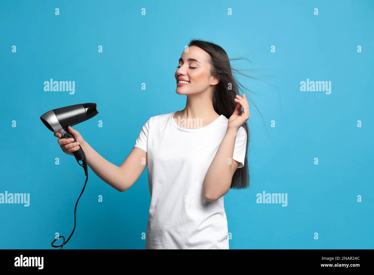 Beautiful young woman using hair dryer on light blue background Stock ...