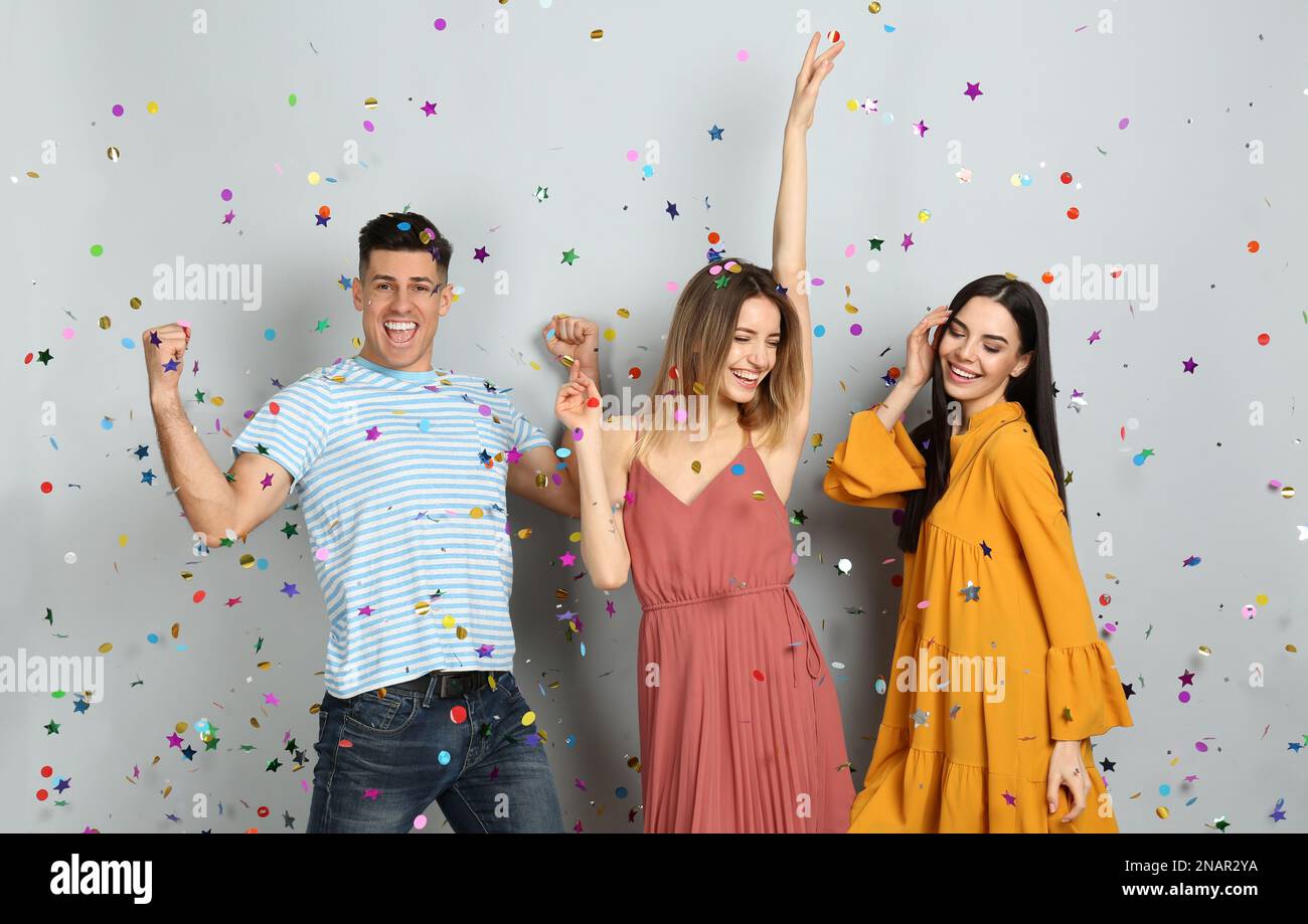 Happy friends and falling confetti on light grey background Stock Photo ...