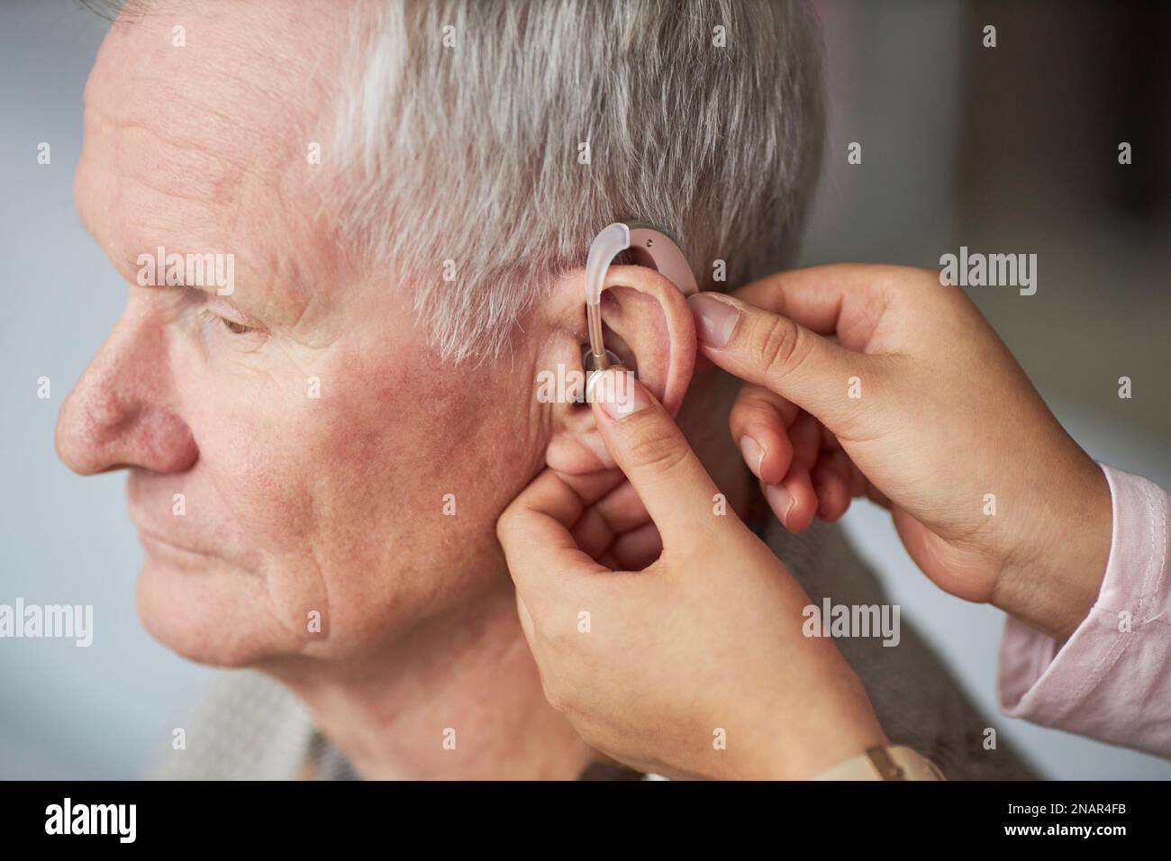 Close-up of social worer helping to wear hearing aid on ear of deaf ...