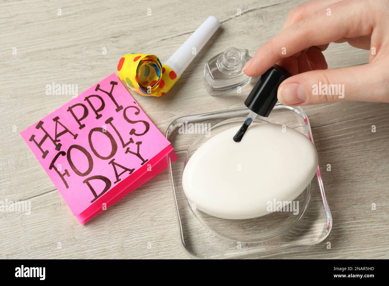 Woman applying transparent nail polish onto soap bar near paper with ...