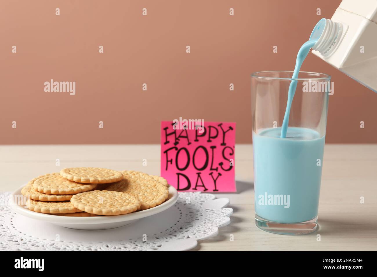 Pouring light blue milk into glass, cookies and words Happy Fool's Day ...