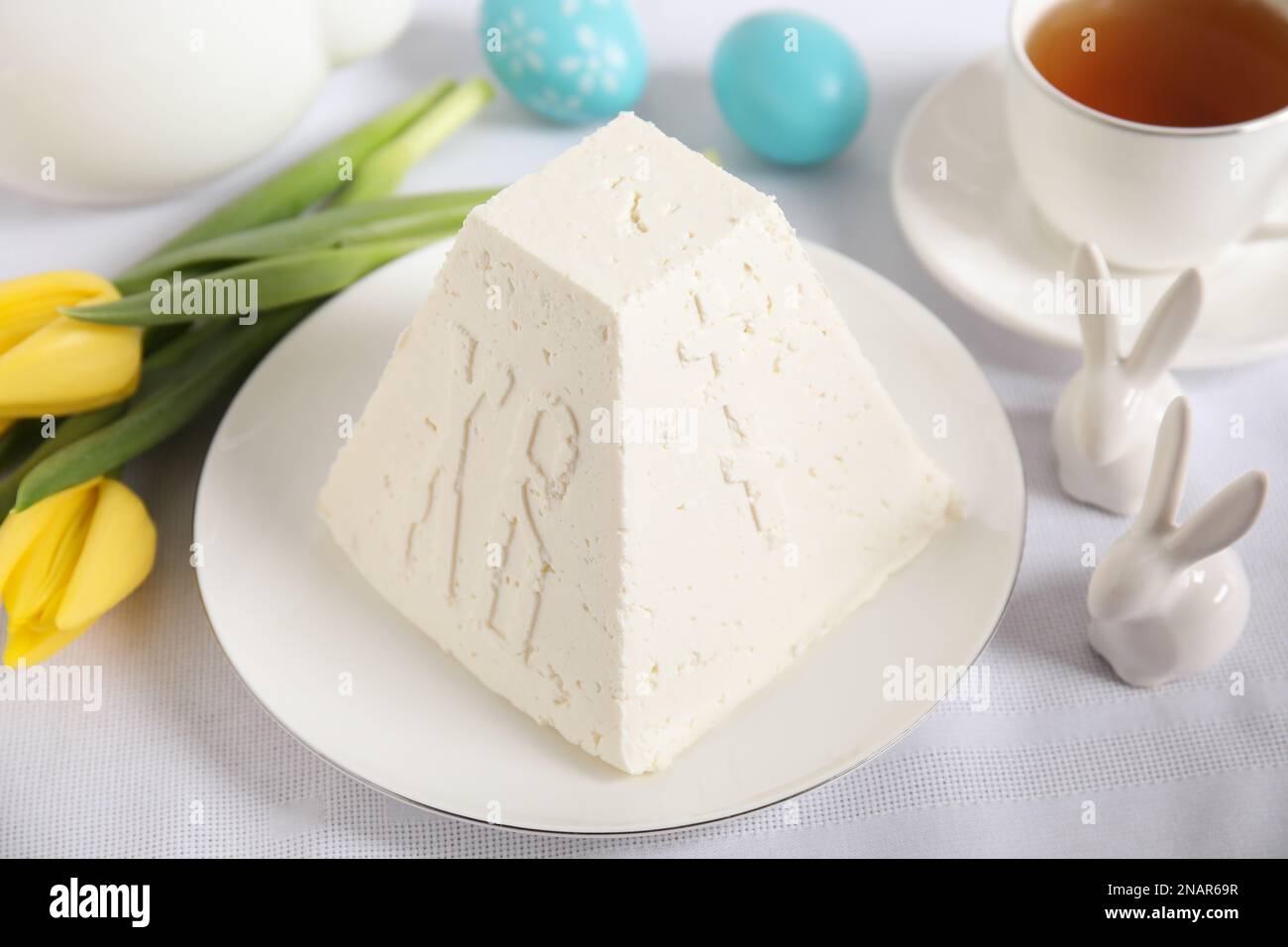 Traditional cottage cheese Easter paskha, decorative bunnies and yellow tulips on white fabric ...