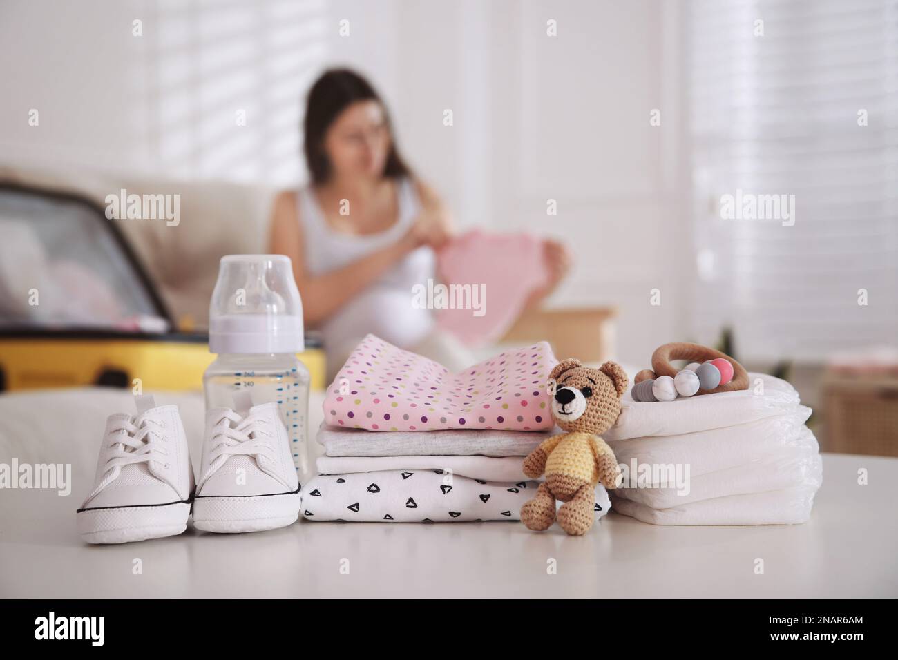Baby clothes with accessories on white table and pregnant woman packing ...