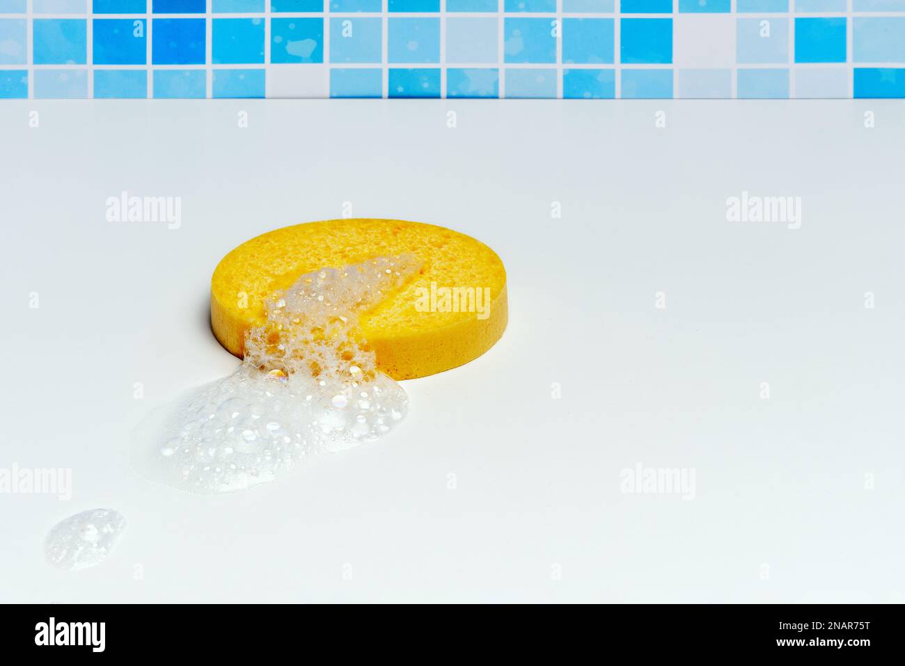 Yellow synthetic bath sponge with foam on a white surface of a blue ...