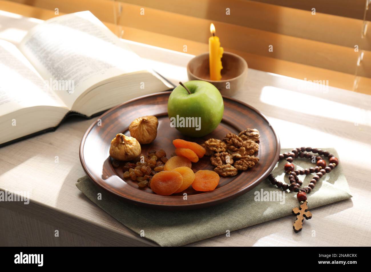 Dried fruits, apple, prayer beads, Bible and candle on window sill ...