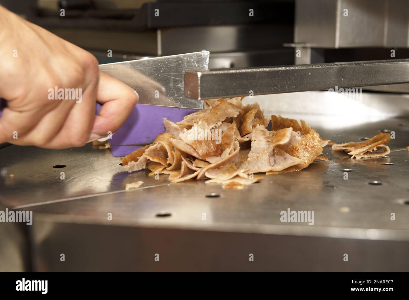 A kebab employee cutting roast lamb meat on the roll to prepare a ...