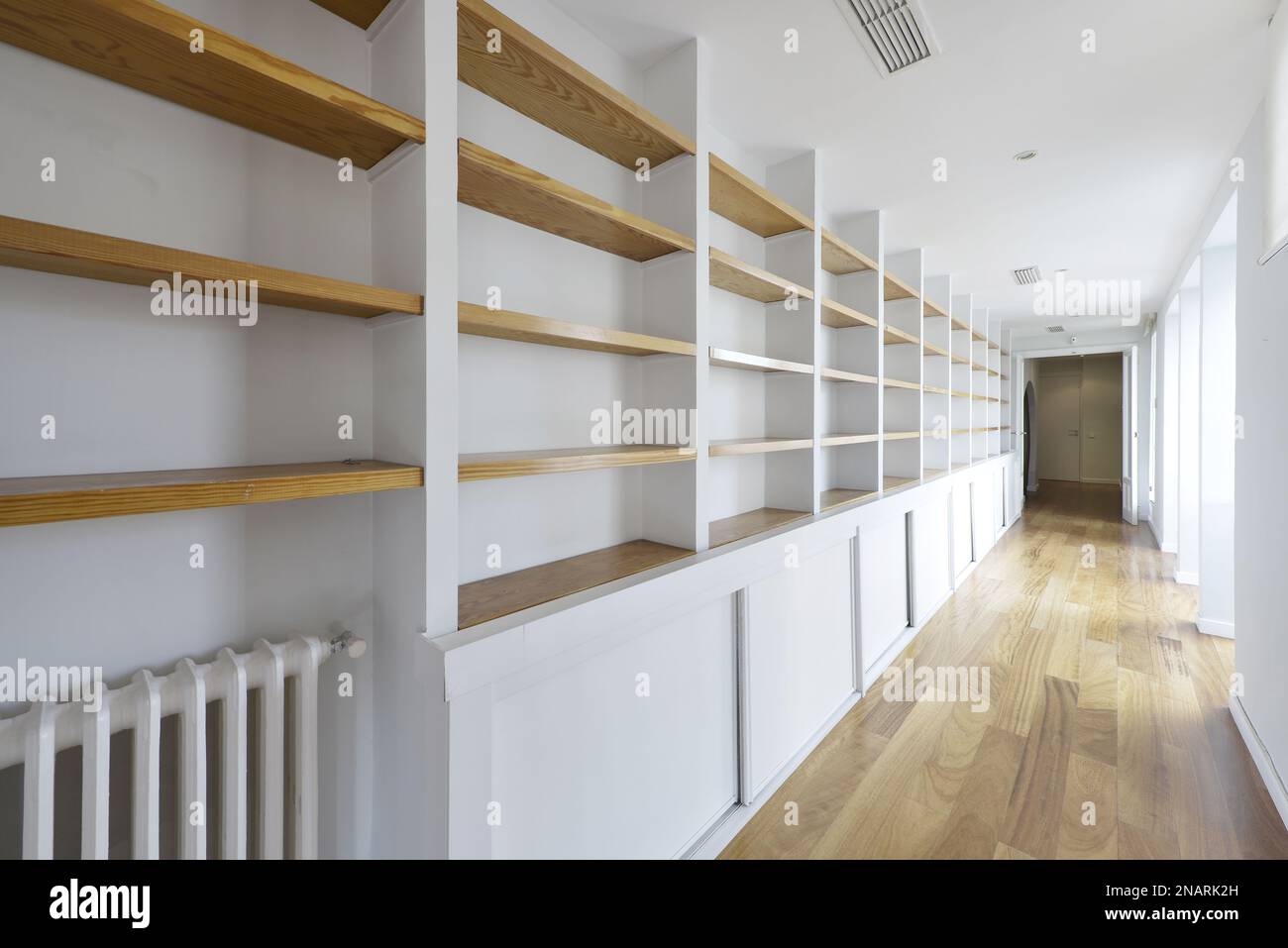 Long hallway of a home with a long empty bookcase with wooden shelving ...