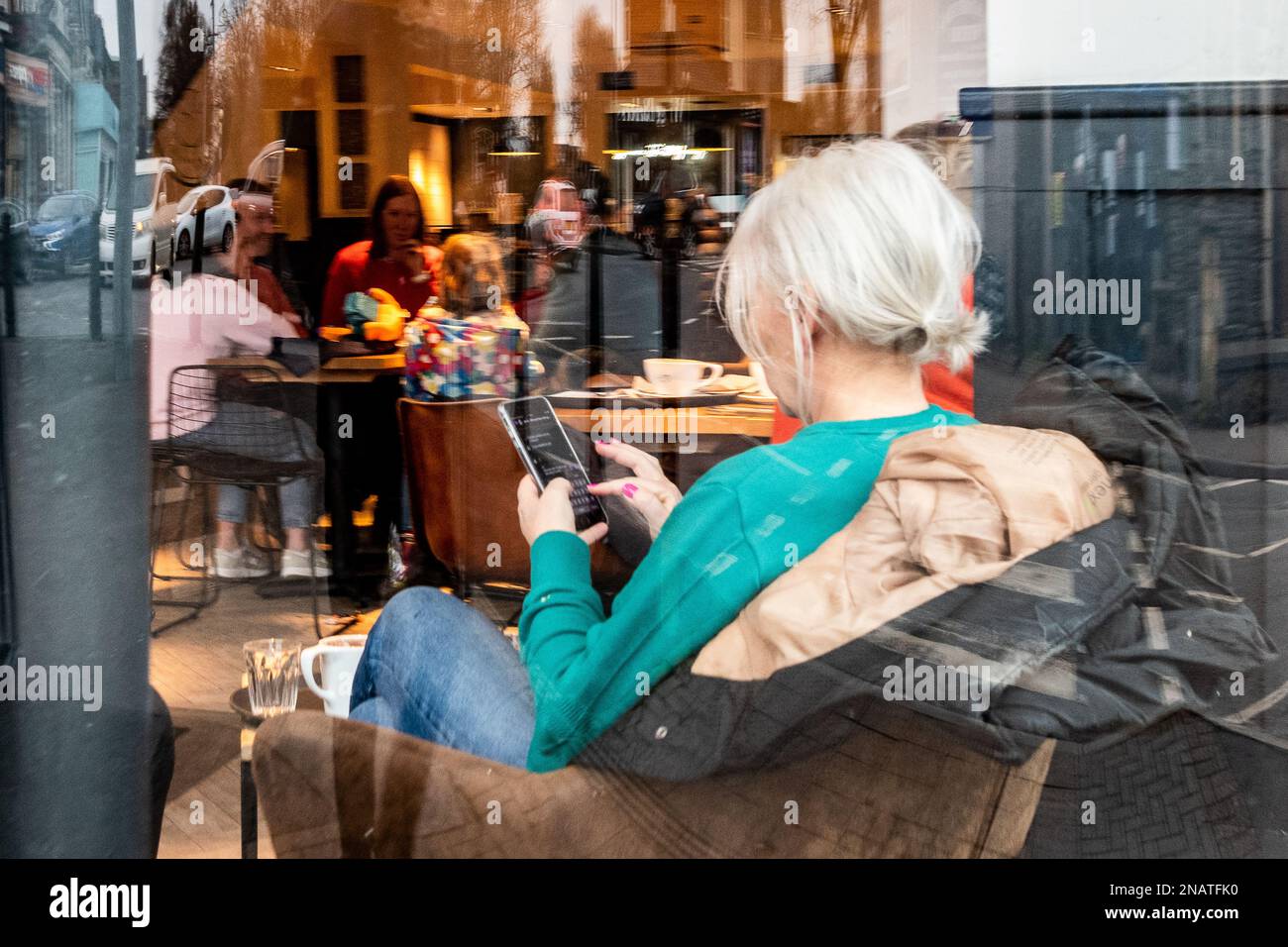 Woman scrolling down messages on her mobile phone inside a cafe ...