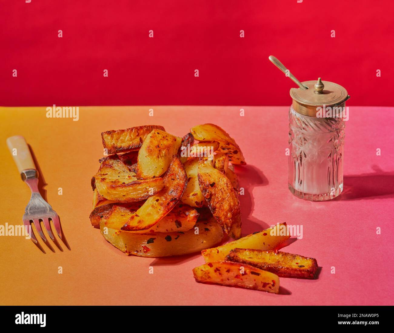 Spicy potato chips on a coloured background with seasoning and a fork ...
