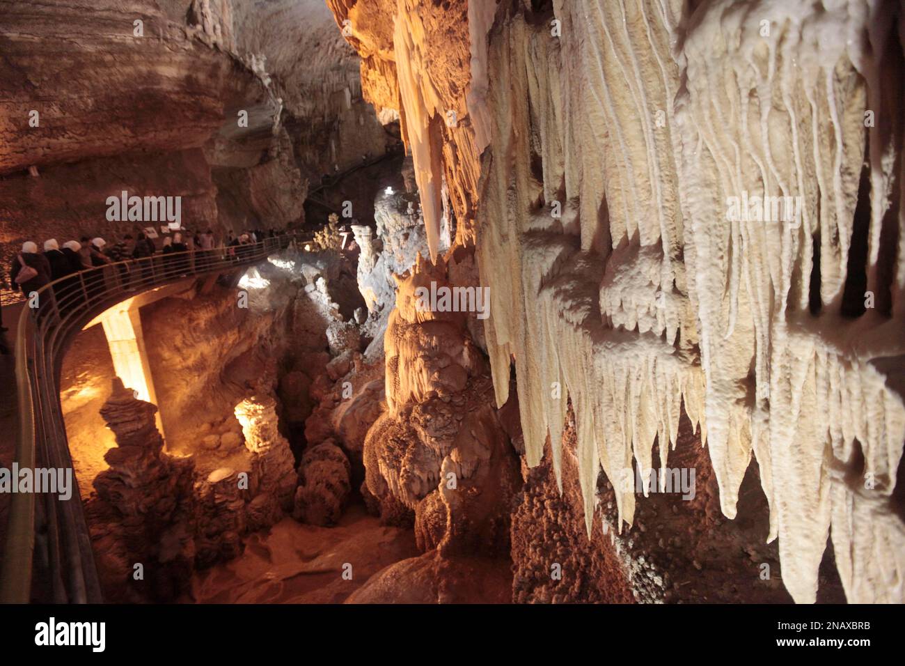 Tourists walk next to stalactites which are seen hanging in the upper ...