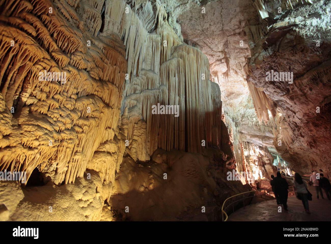 Tourists walk next to stalactites which are seen hanging in the upper ...