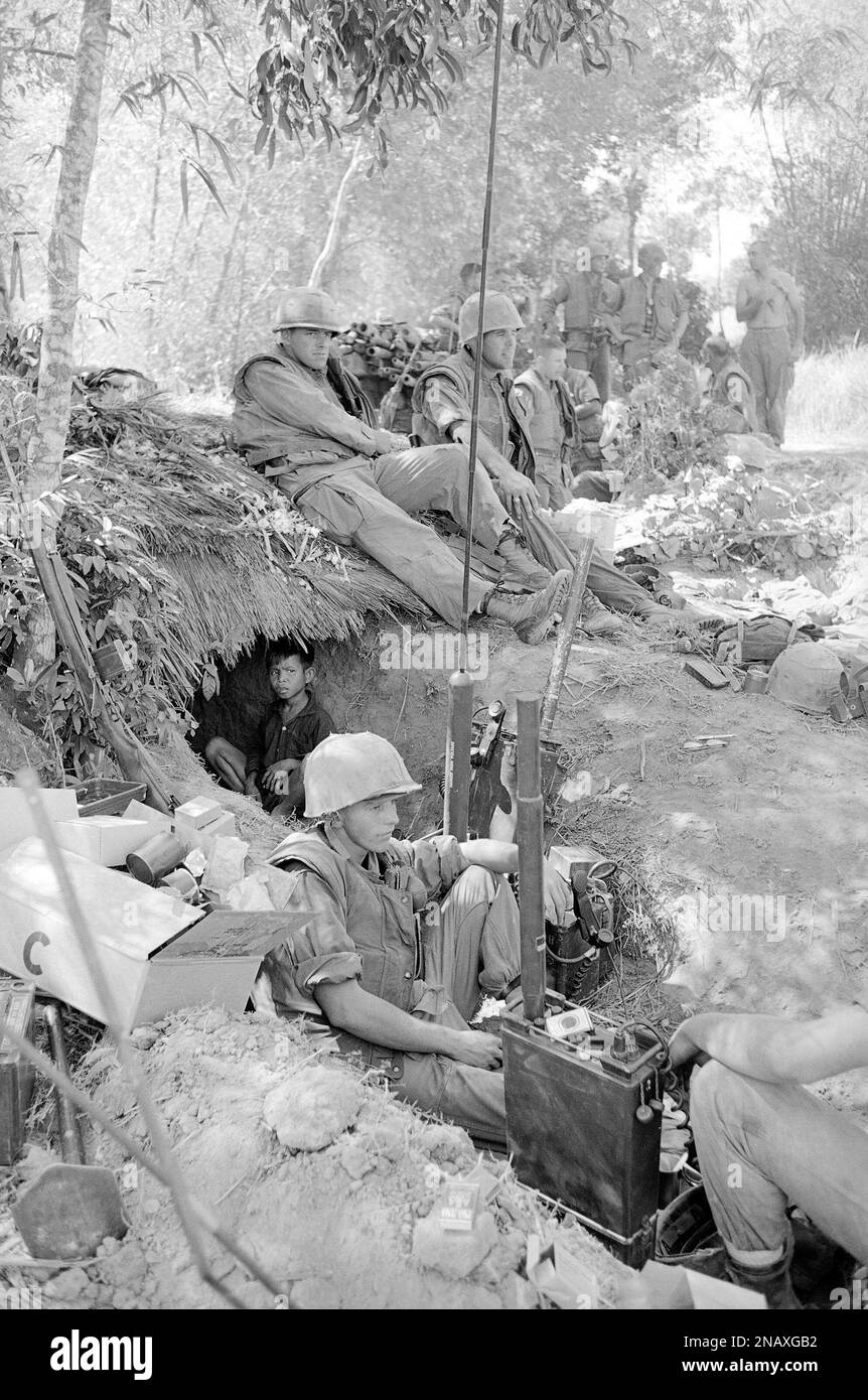 Burly U.S. Marines rest around bunker as young Vietnamese boy sits ...