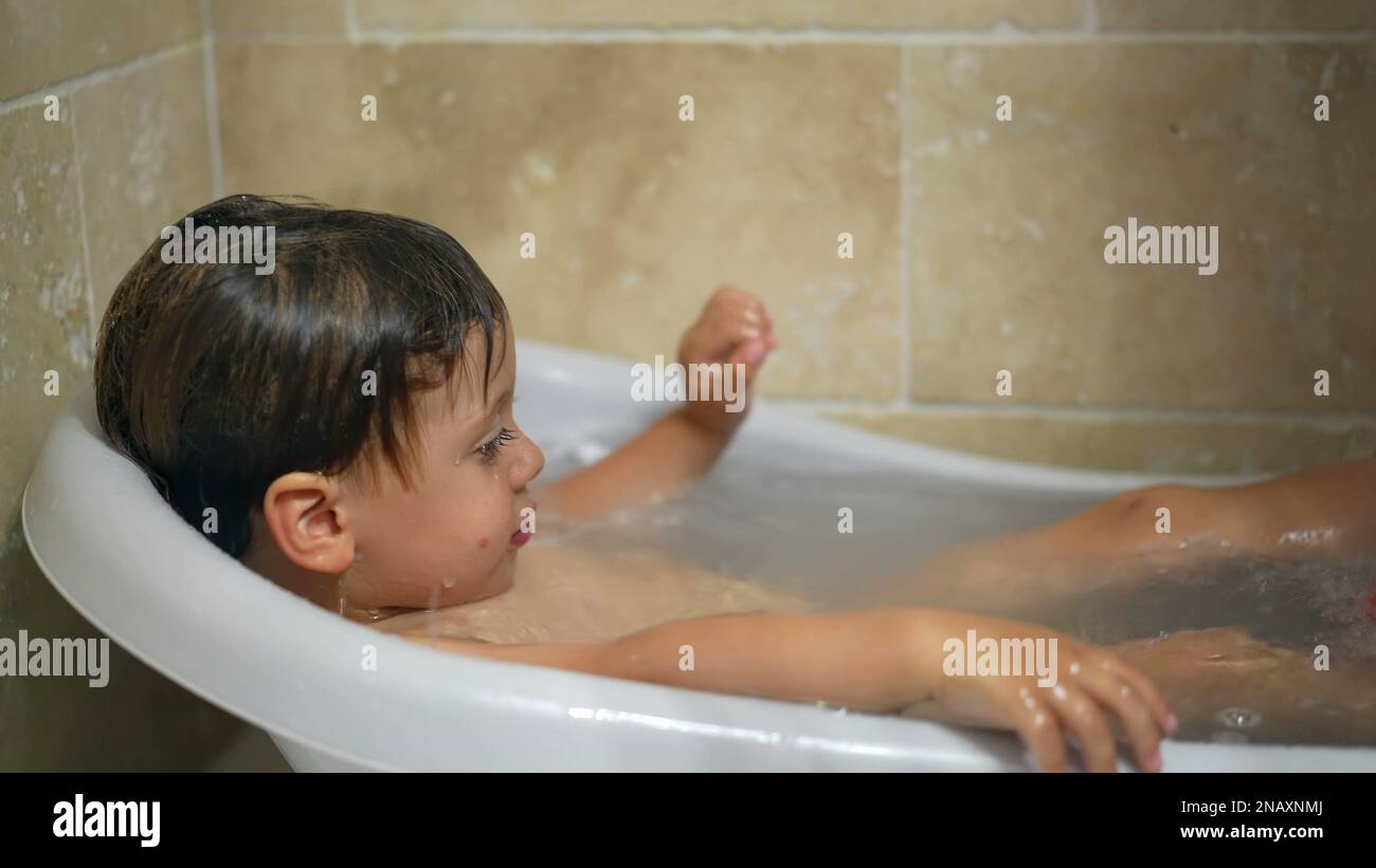 Cute baby bathing in small bathtub. Toddler boy washing routine bath ...
