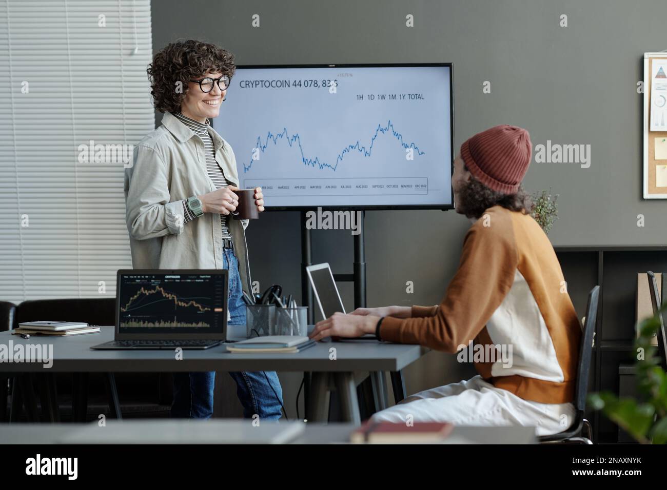 Happy young female economist with cup of coffee talking to male ...
