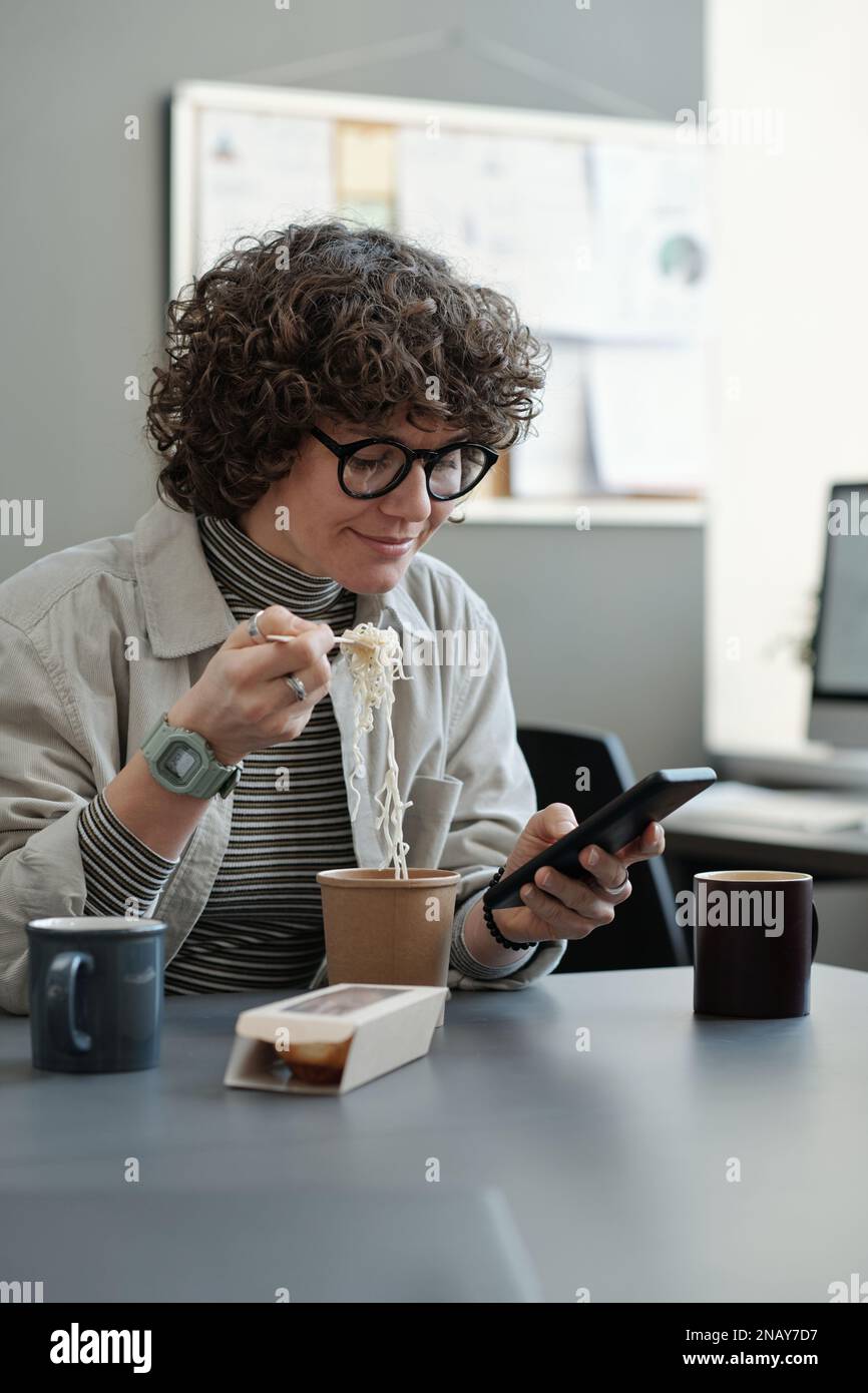 Young hungry and busy female employee eating Chinese wok and texting in ...
