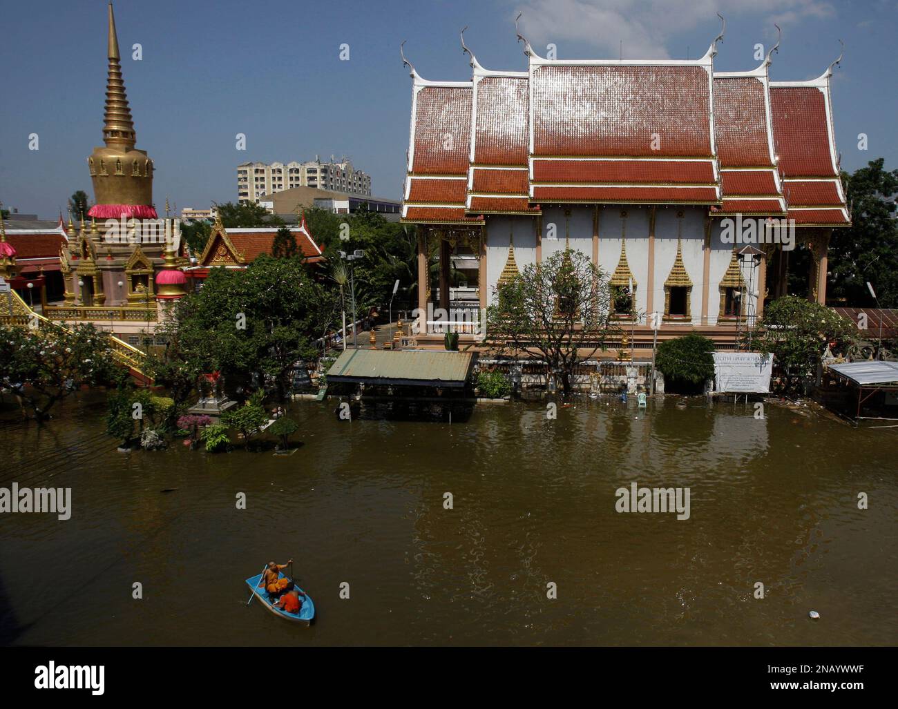 Thai monks use a boat to cross a flooded area at a temple in Bangkok's ...