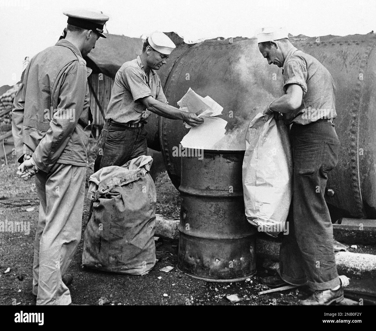 Under the watchful eye of an officer, two sailors burn all secret ...