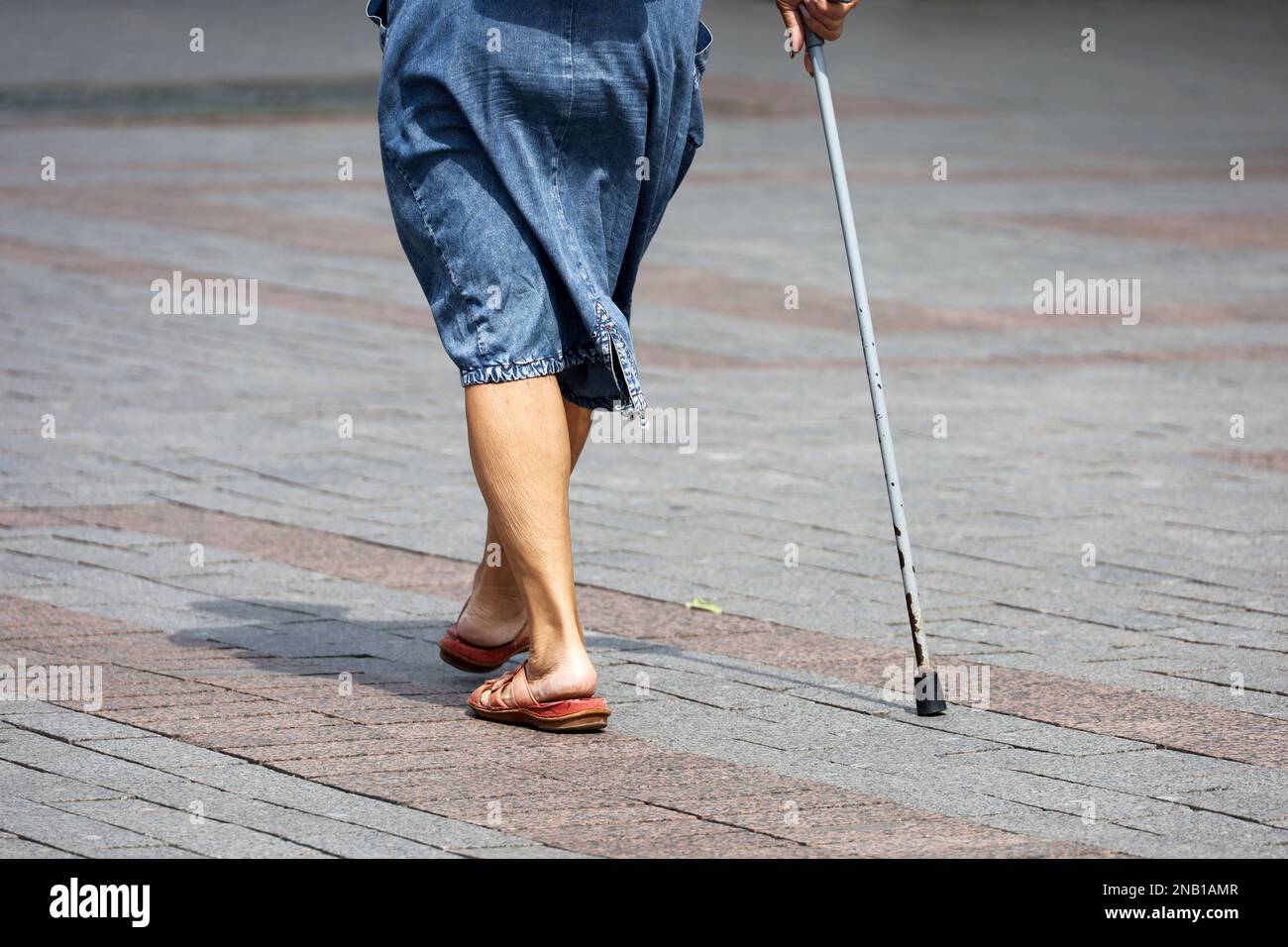 Elderly woman walking with cane on city street, legs on sidewalk ...