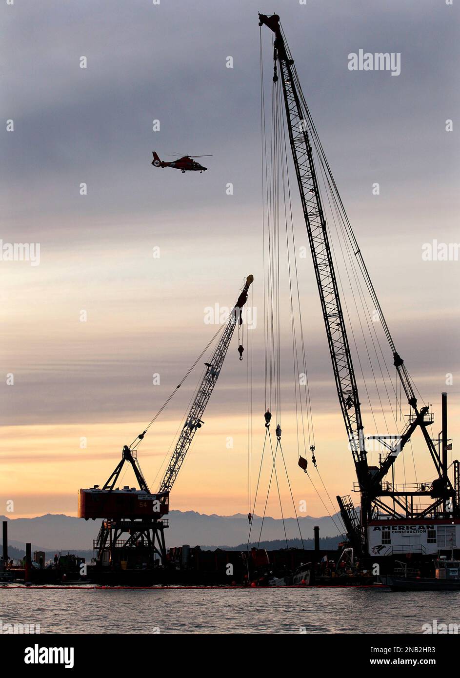 A U.S. Coast Guard helicopter flies past as cranes and barges surround ...