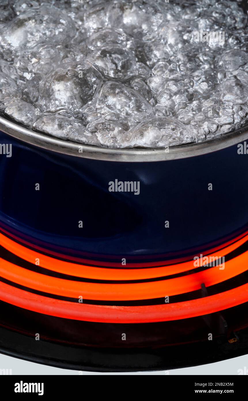 Vertical close-up shot of a blue pot on a stove top on a red hot burner ...