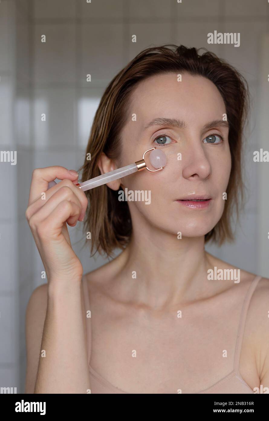 Woman massages her face with rose quartz massager. Self care routine ...