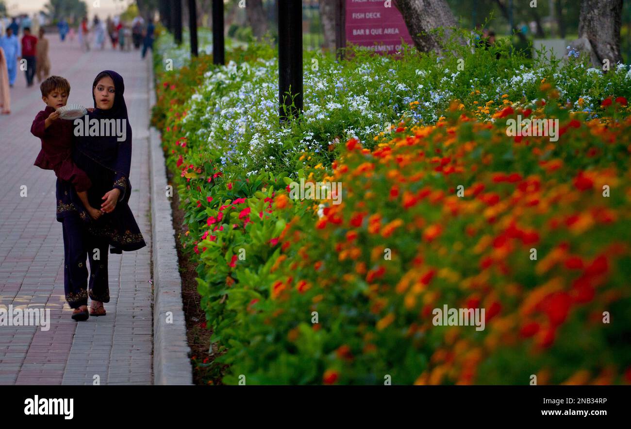 A Pakistani girl carries her younger brother as she walks at a park in ...