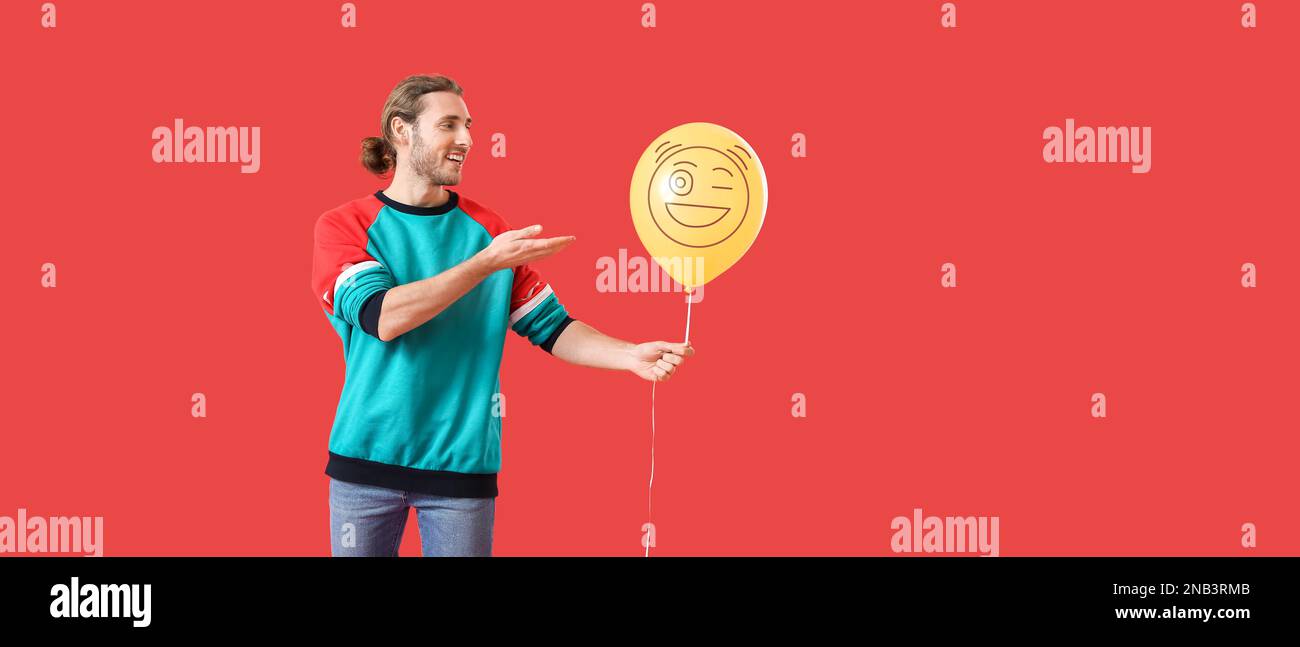 Handsome young man and balloon with drawn happy emoticon on red ...