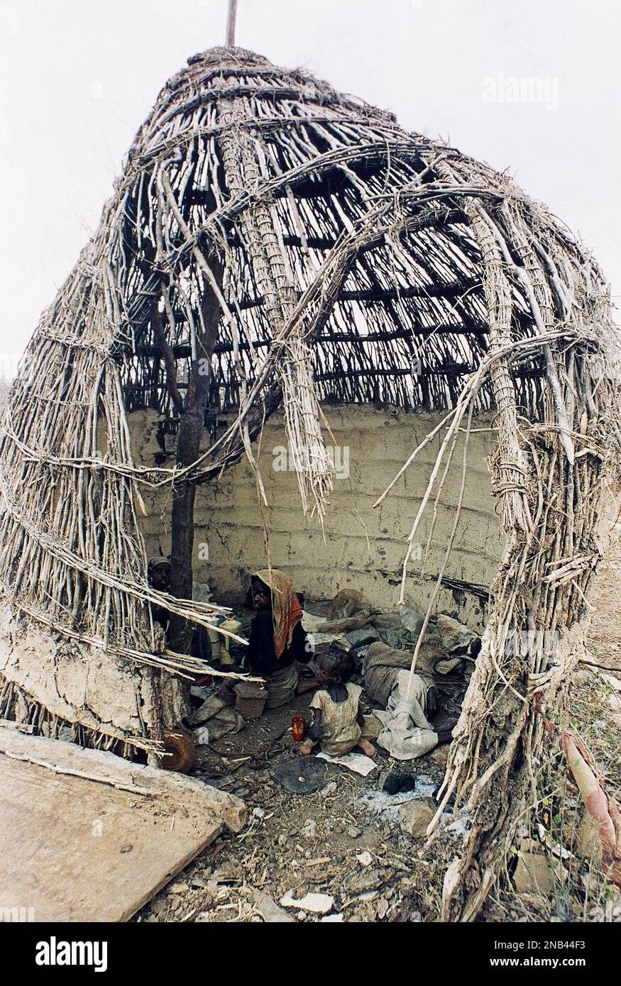 Villagers rest and eat in a partially destroyed hut in the village of ...