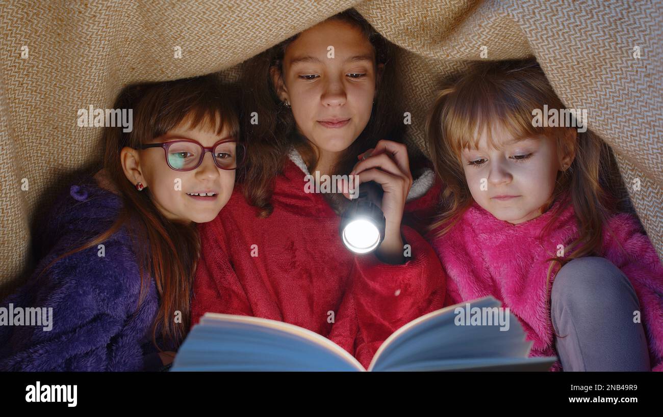 Teen girl and toddler child sisters under blanket plaid covers with ...