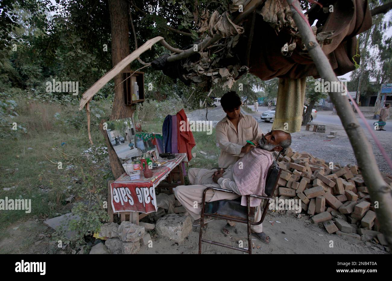 A Pakistani street barber shaves a customer's beard on a roadside in ...