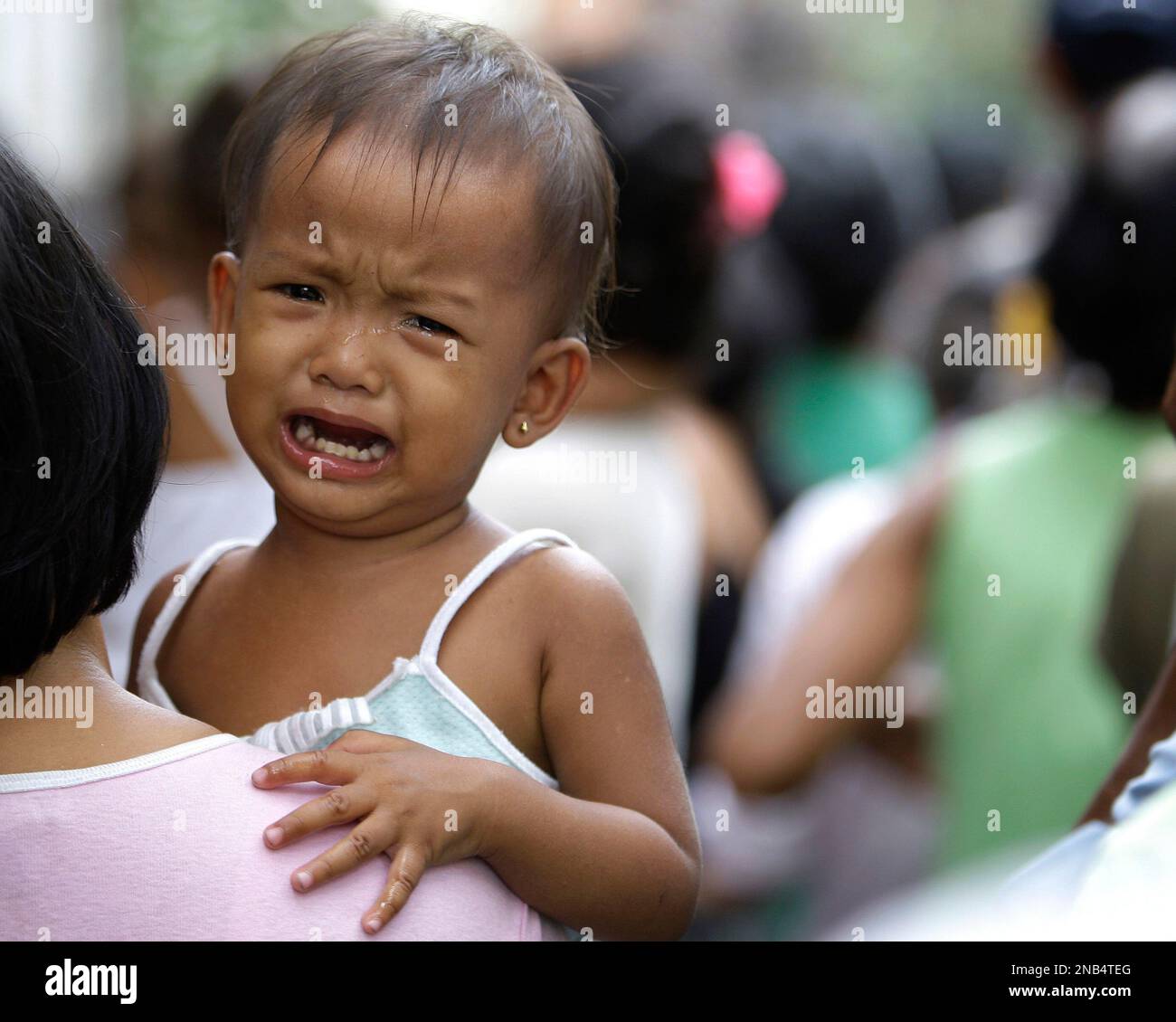 A Filipino girl cries as she is carried by her mother at a long cue for ...