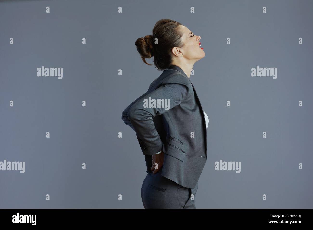 tired stylish 40 years old woman employee in grey suit having back pain ...