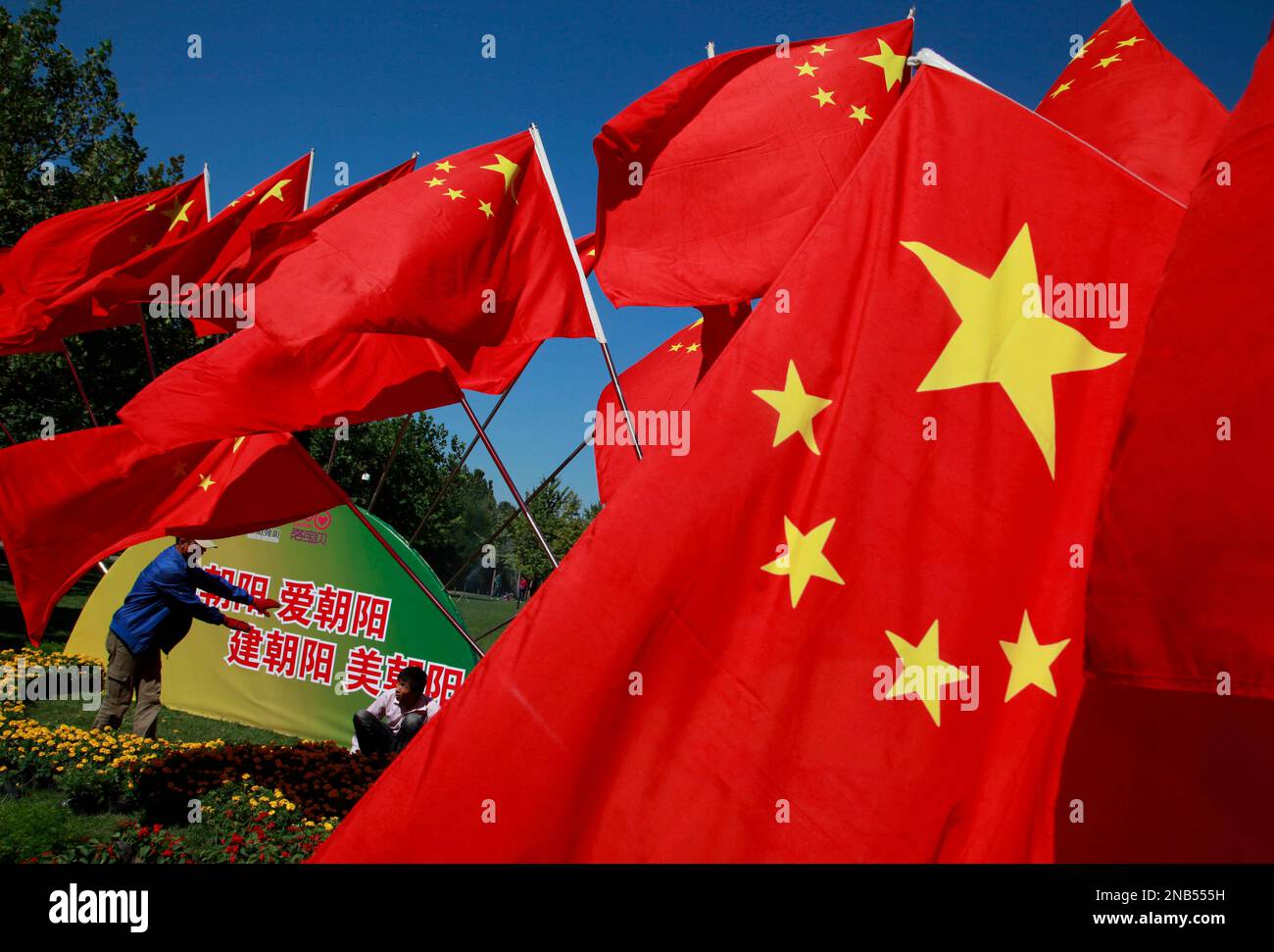 Workers arrange pots of plants near Chinese national flags set up ahead ...