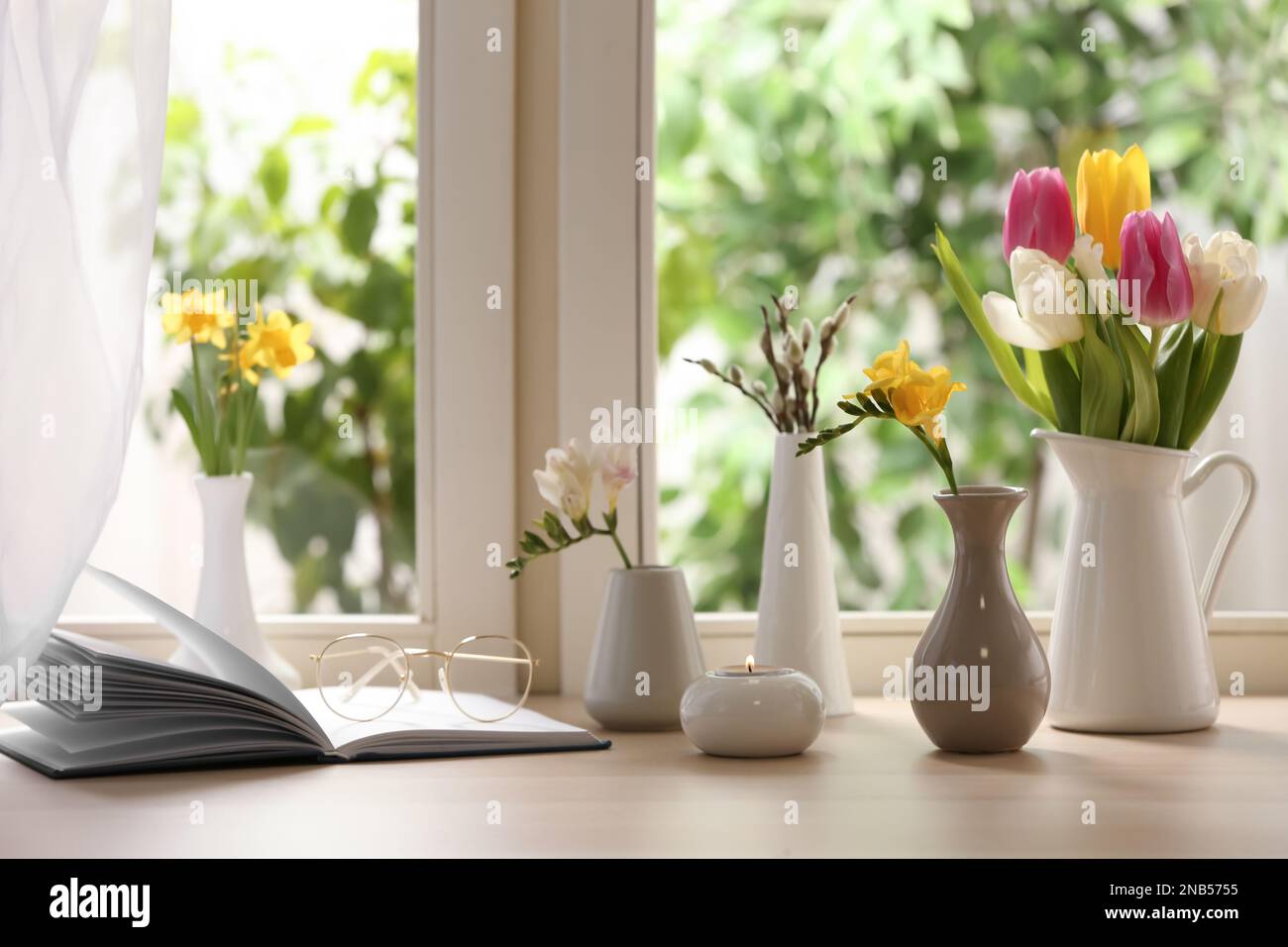 Different beautiful spring flowers, burning candle and book on window ...