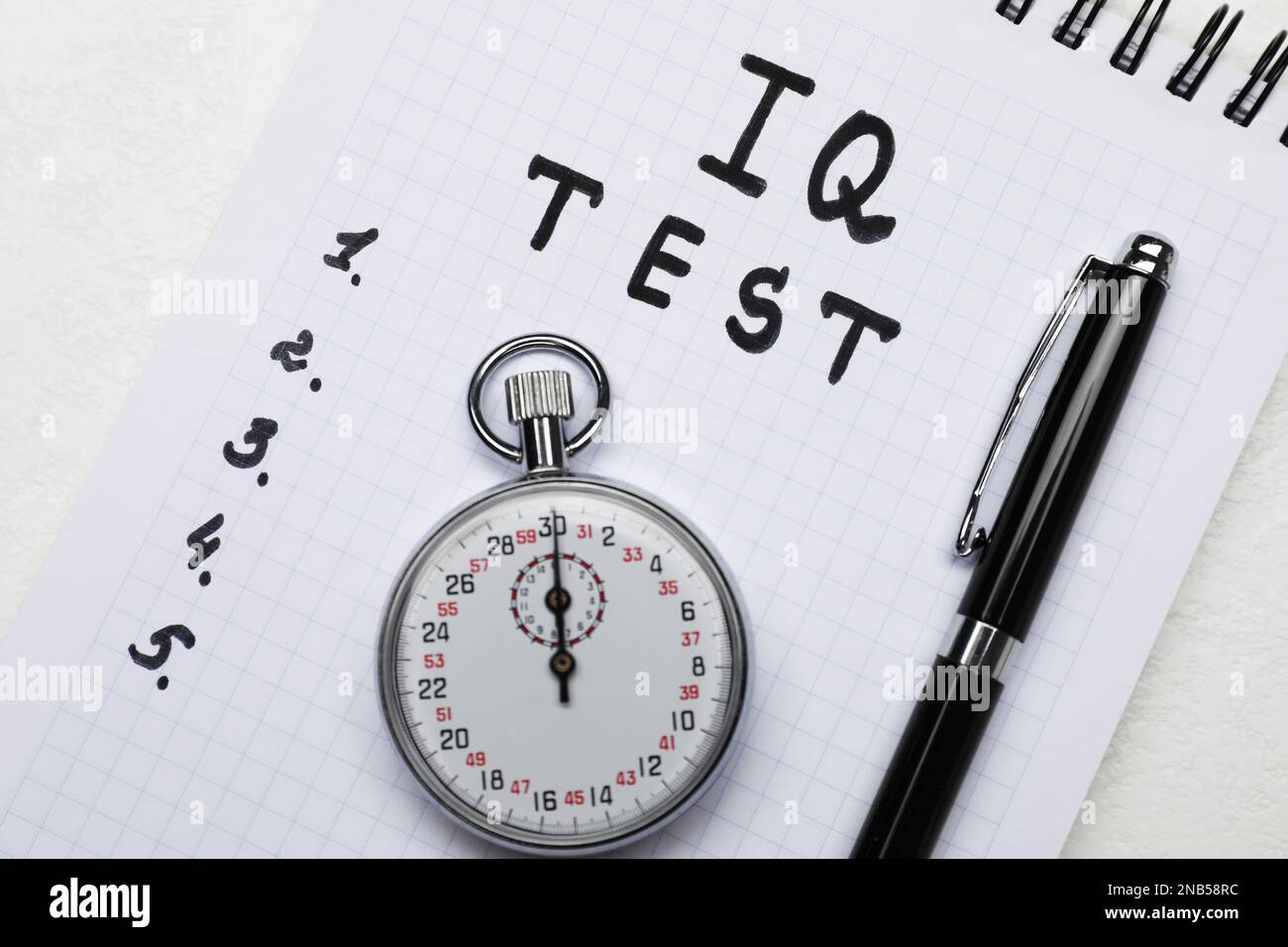 Notebook with words IQ Test, pen and timer on white table, top view ...